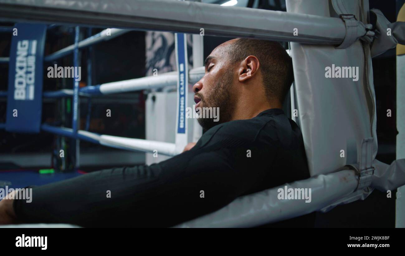 Tired and exhausted African American boxer sits in boxing ring corner ...