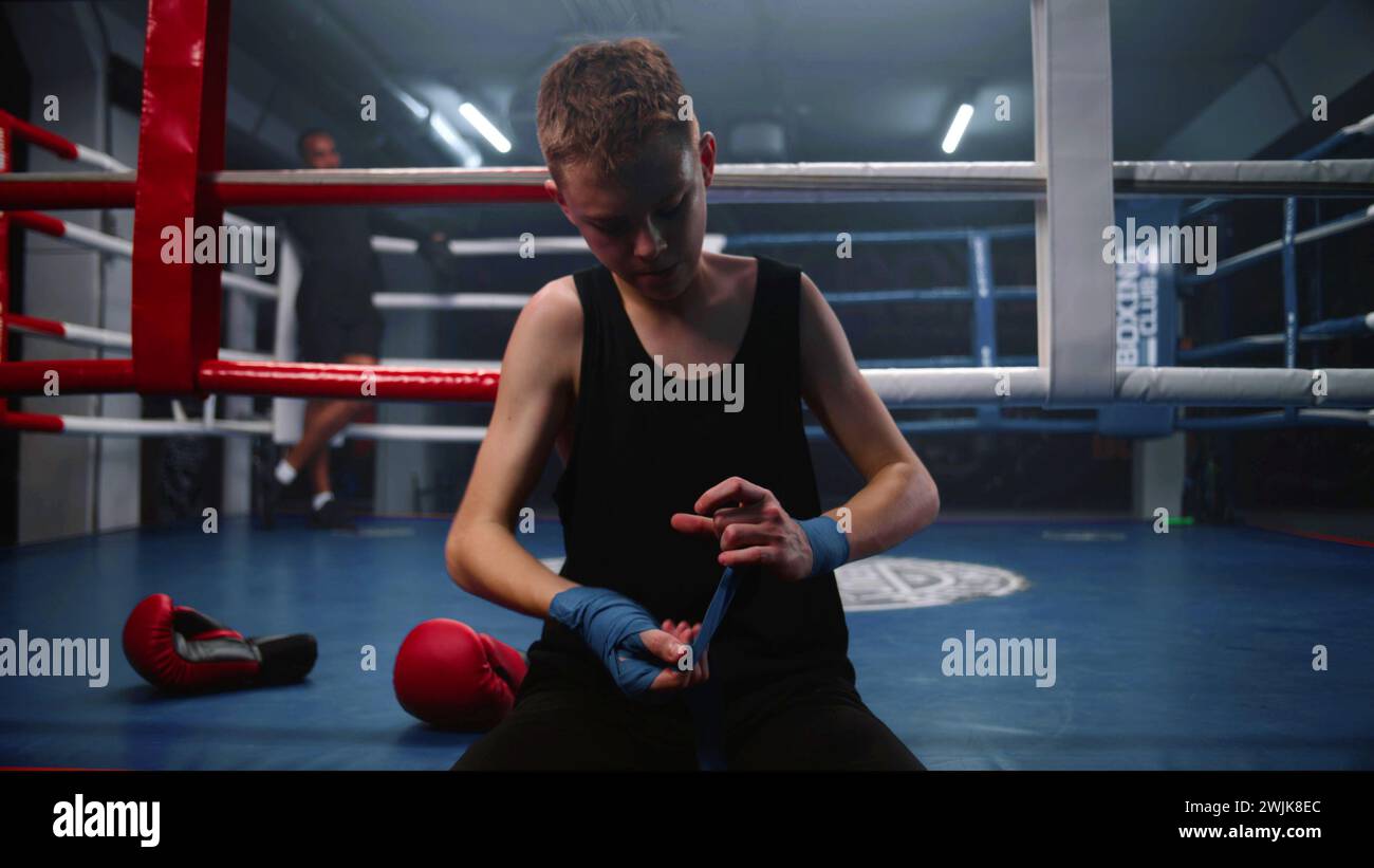 Young boxer sits near boxing ring and wraps his hands with bandage for ...