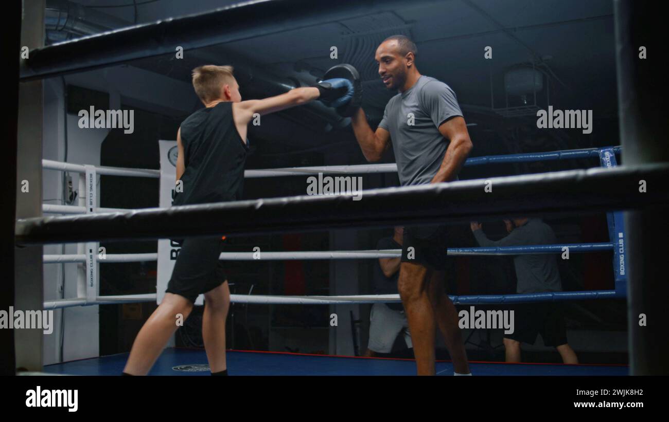 Young boy in boxing gloves hits punching mitts and practices on boxing ...