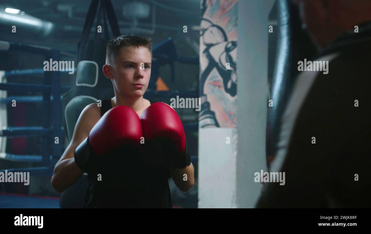 Confident young fighter hits punching bags while training in dark ...