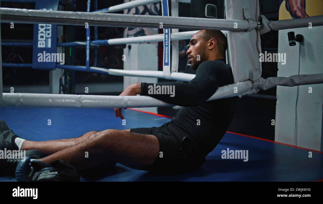 Tired and exhausted African American fighter sits in boxing ring corner ...