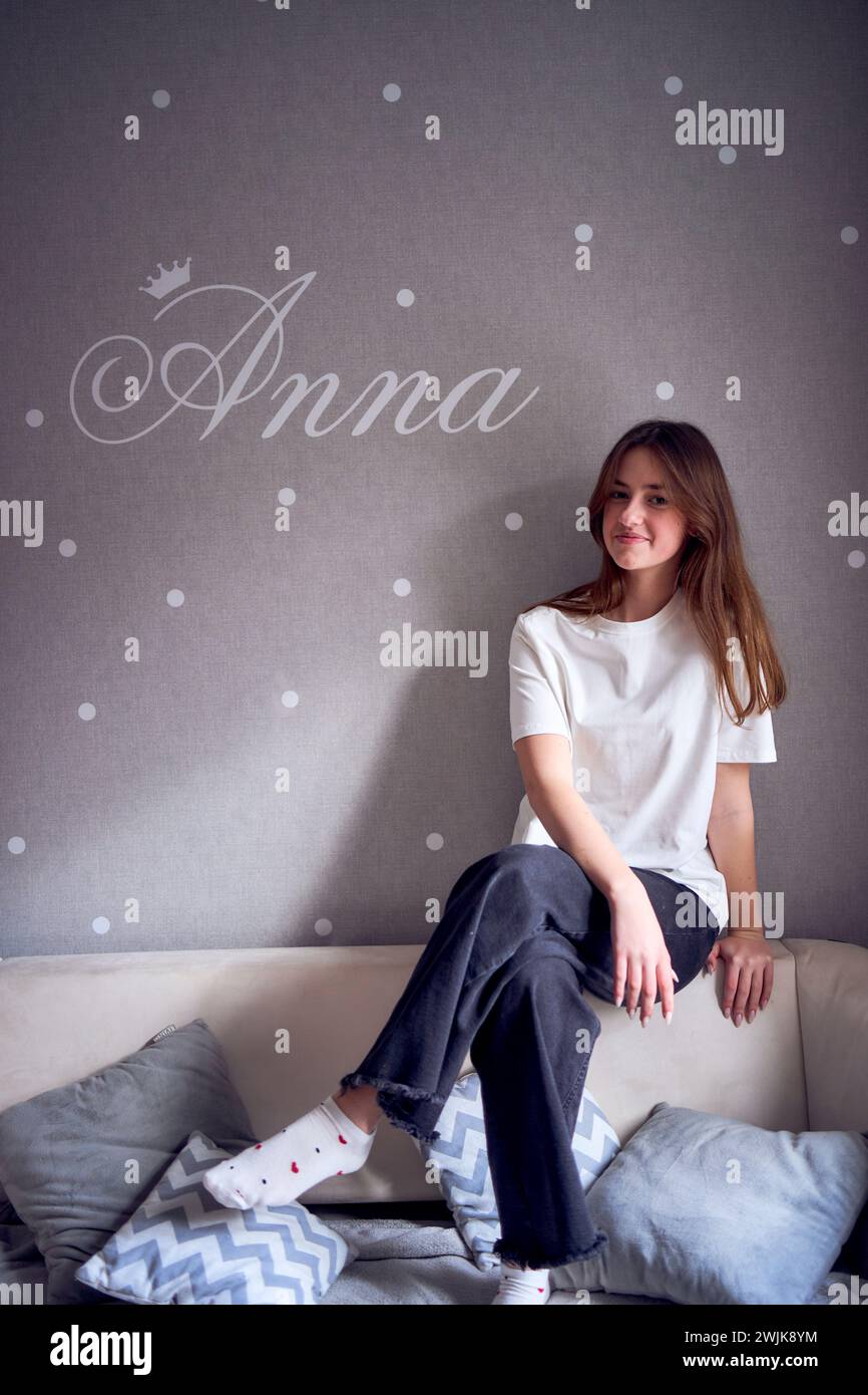 beautiful teenage girl sits on a bed near the wall with her name ...