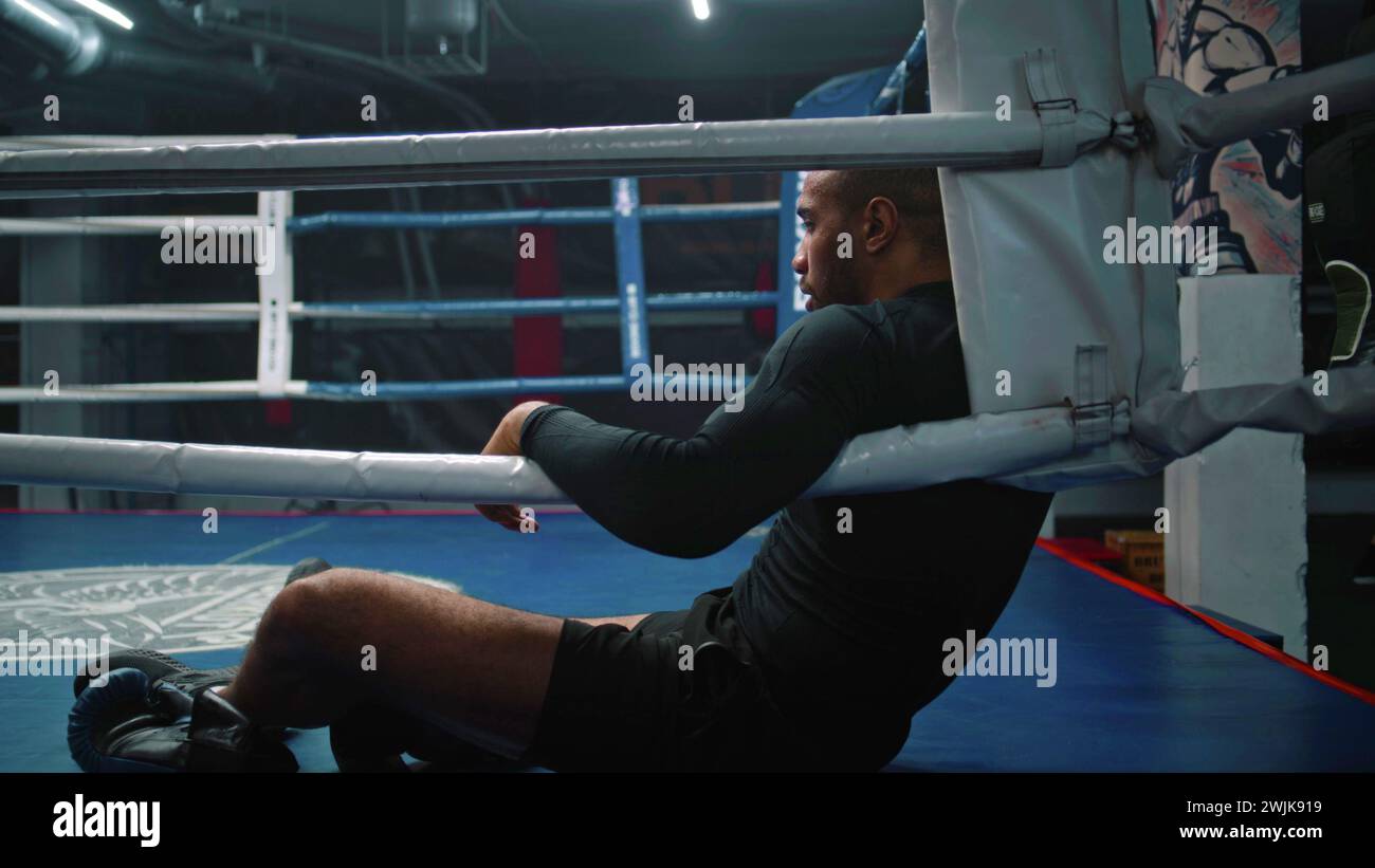 Tired and exhausted African American boxer sits in boxing ring corner ...