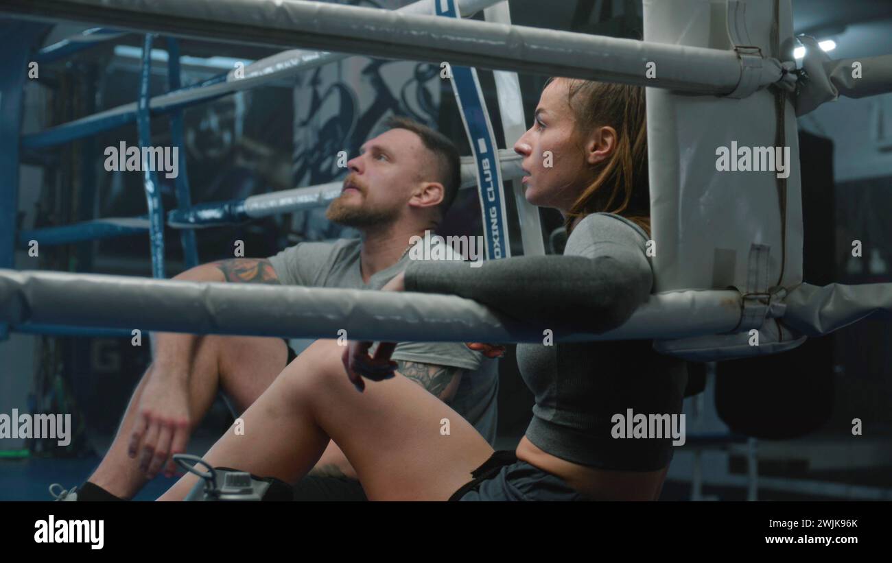 Tired woman sits at ring corner, takes off boxing gloves and starts ...
