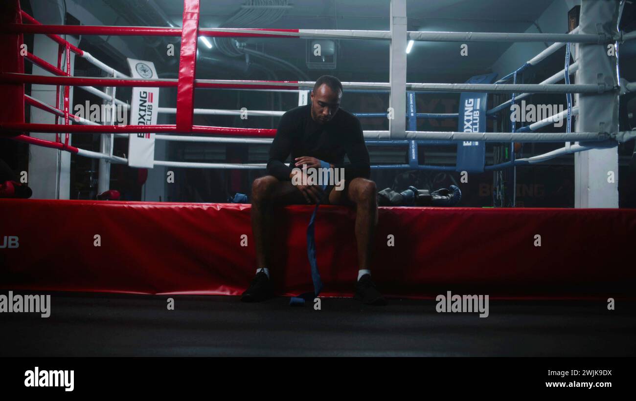 African American boxer sits near boxing ring and wraps his hands with ...