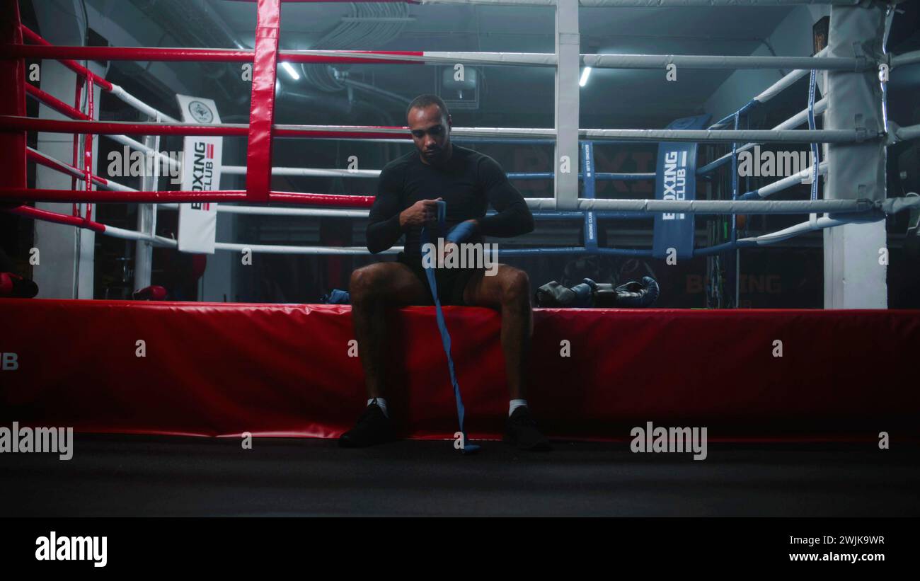 African American boxer sits near boxing ring and wraps his hands with ...