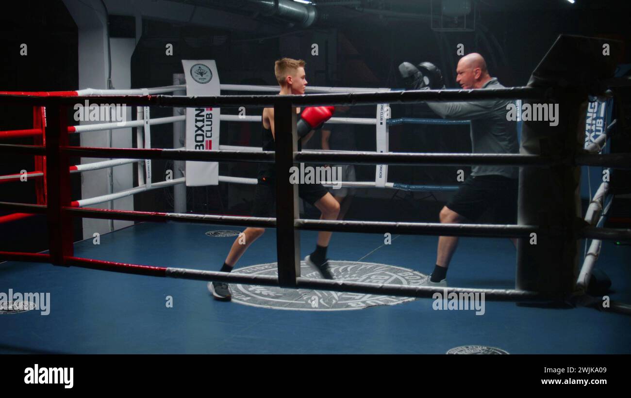 Teenager in boxing gloves trains and exercises with adult trainer on ...