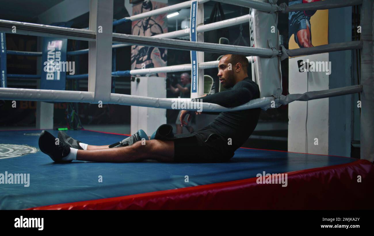 Tired and exhausted African American fighter sits in boxing ring corner ...