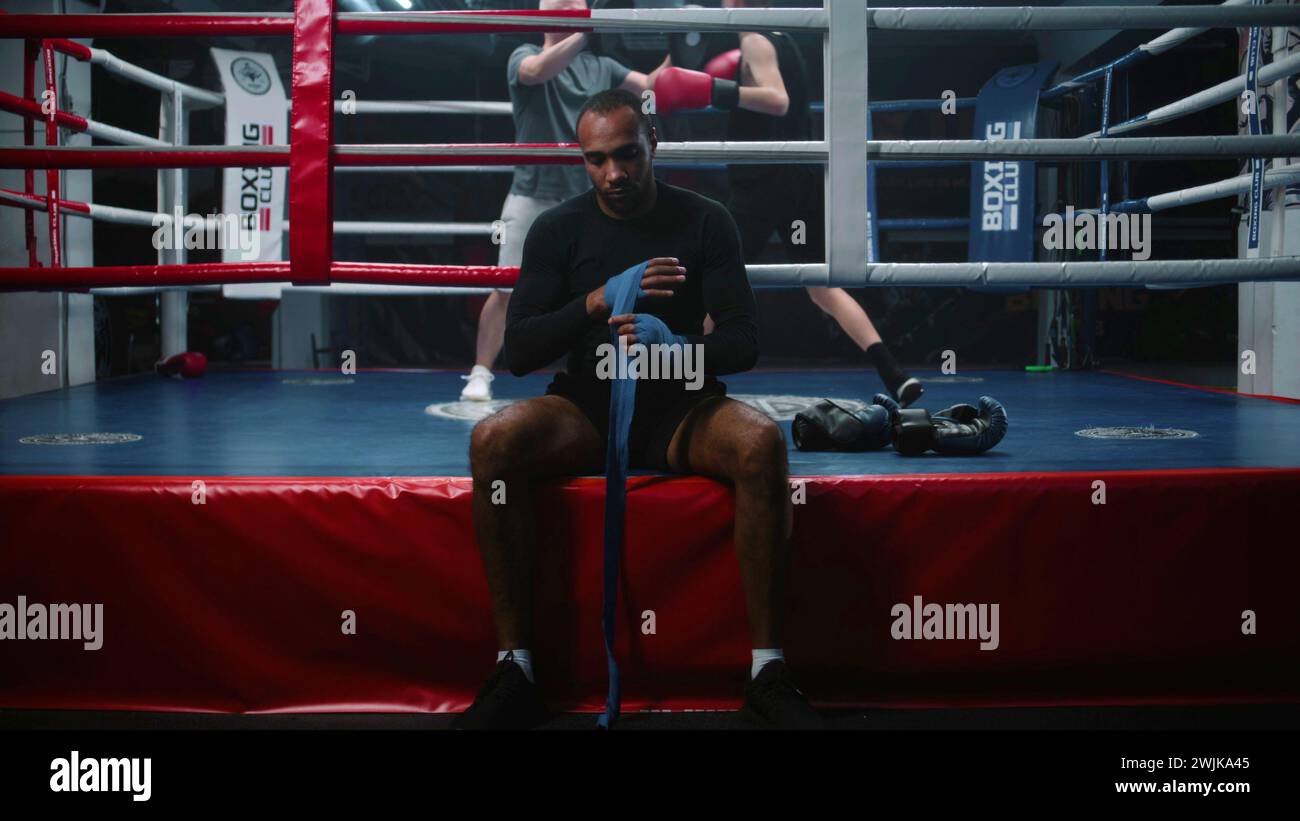 African American boxer sits near boxing ring and wraps hands with ...