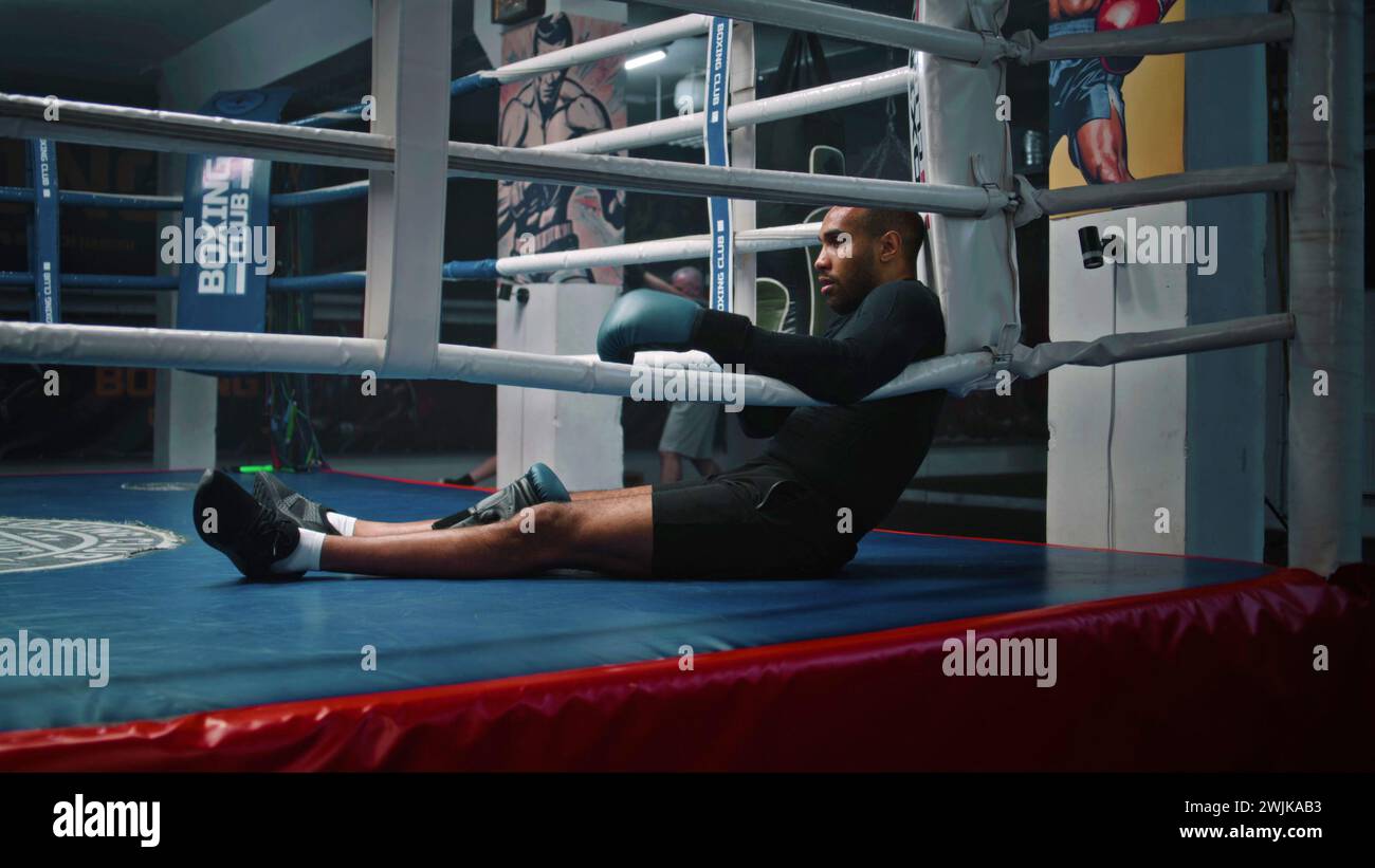 Tired and exhausted African American fighter sits in boxing ring corner ...