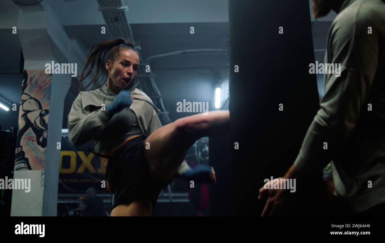 Female fighter in boxing bandages exercises with male trainer in dark ...