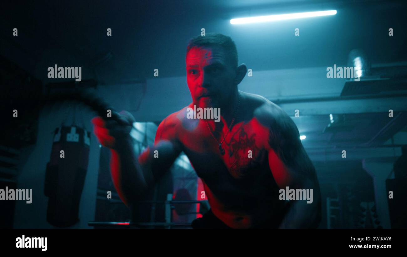 Male athlete exercises with battle ropes in dark boxing gym with LED ...