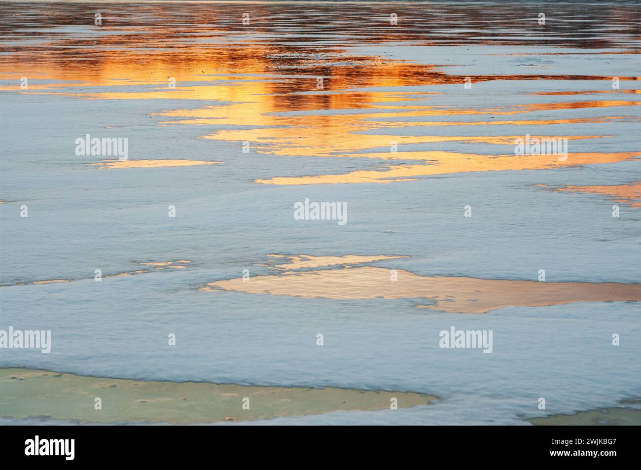 The icy lake shines with the warm hues of a calm sunset, showcasing the ...