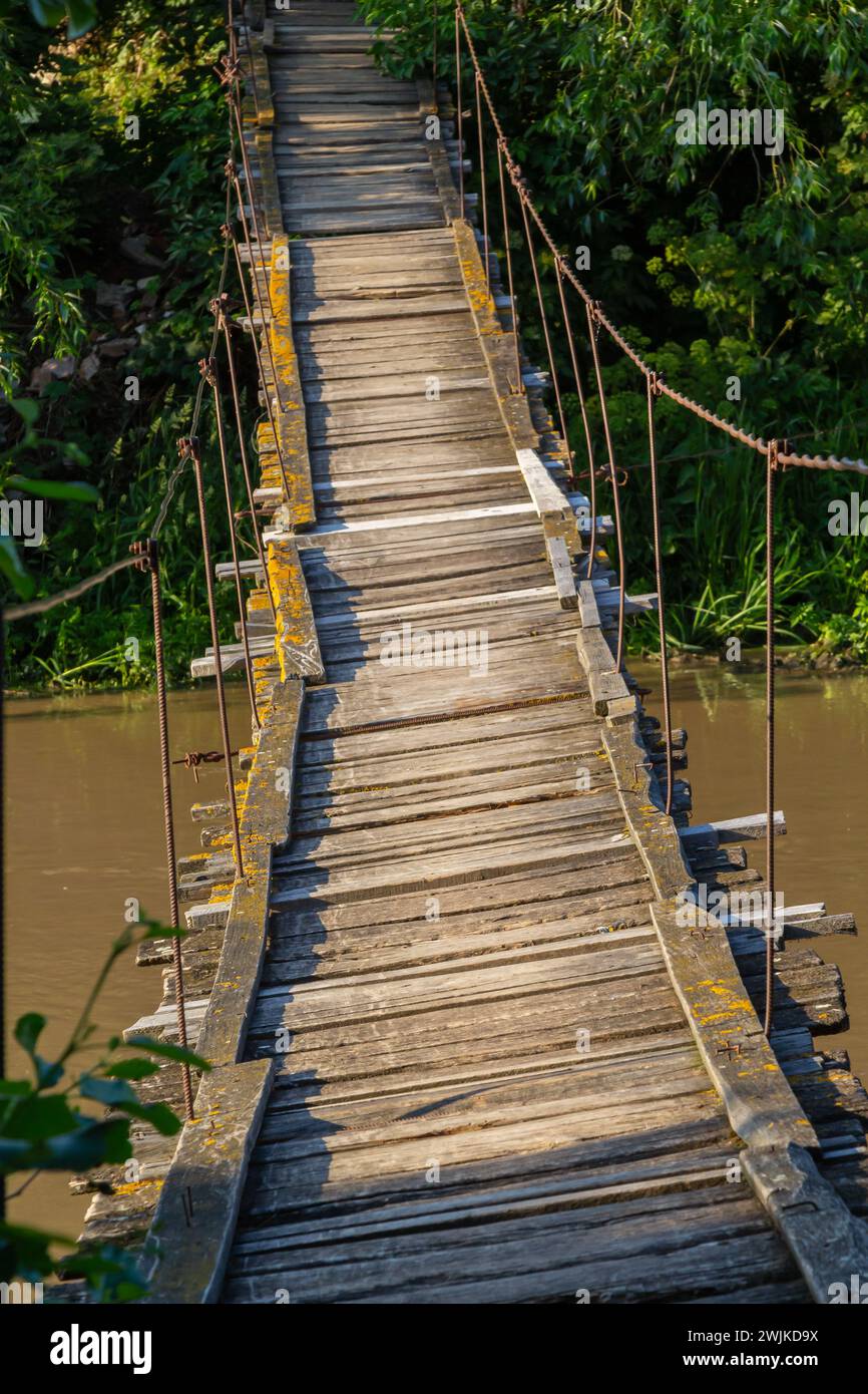 old suspension bridge over the river in the countryside going into ...