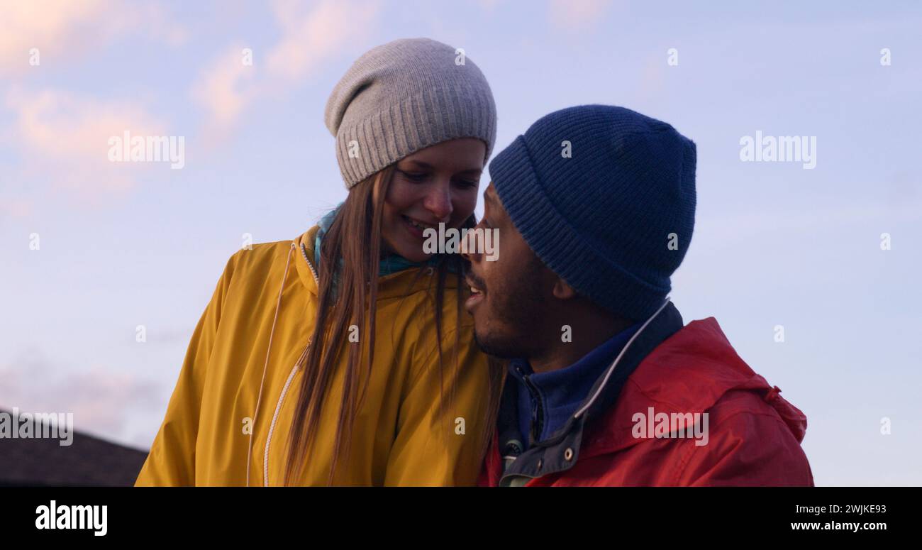 Happy multiethnic couple smiles and hugs, looks at beautiful sunset ...
