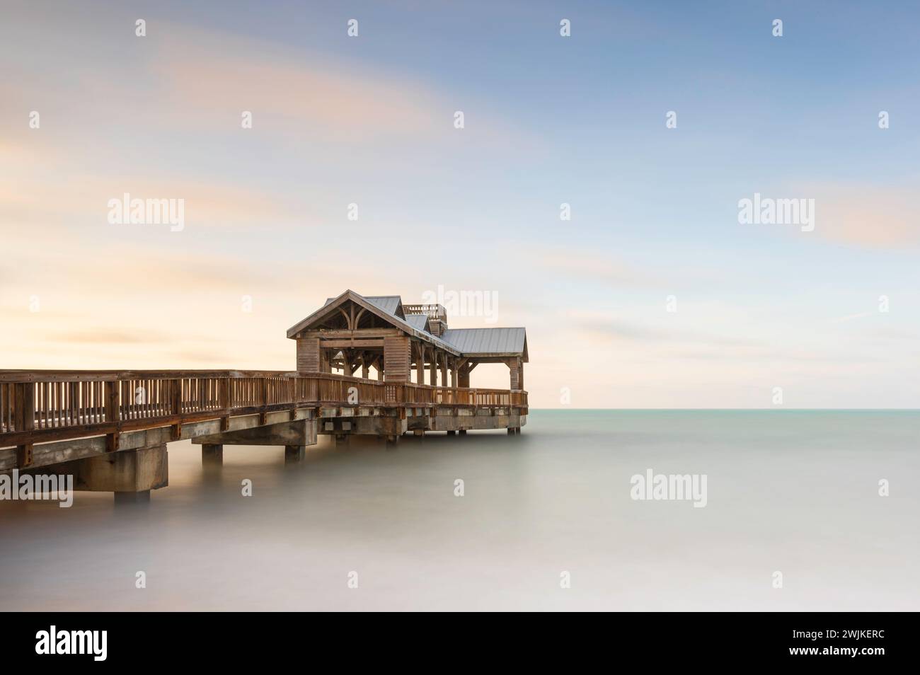 A wooden pier, reaching out into a totally smooth, calm ocean, at ...