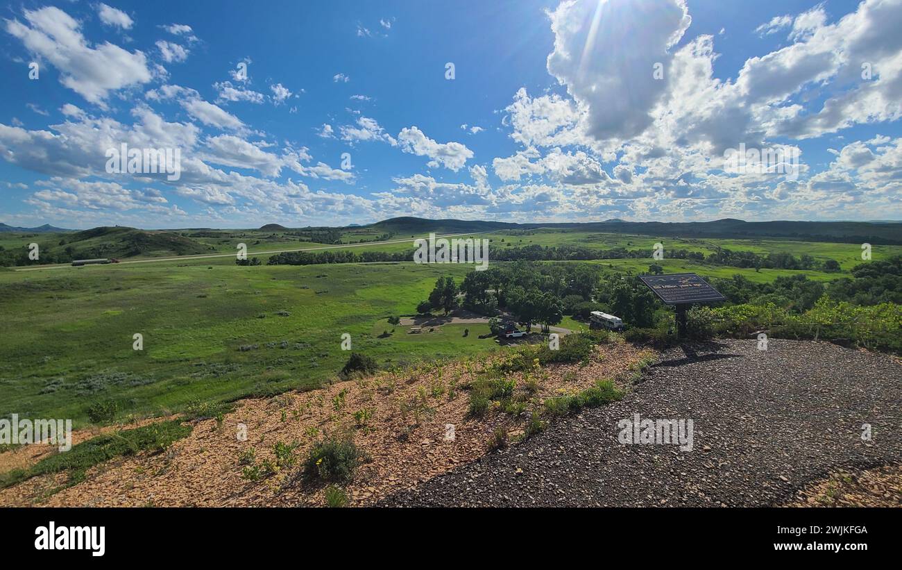 A vast expanse of vibrant green field stretches out before a backdrop of dirt roads and lush ...