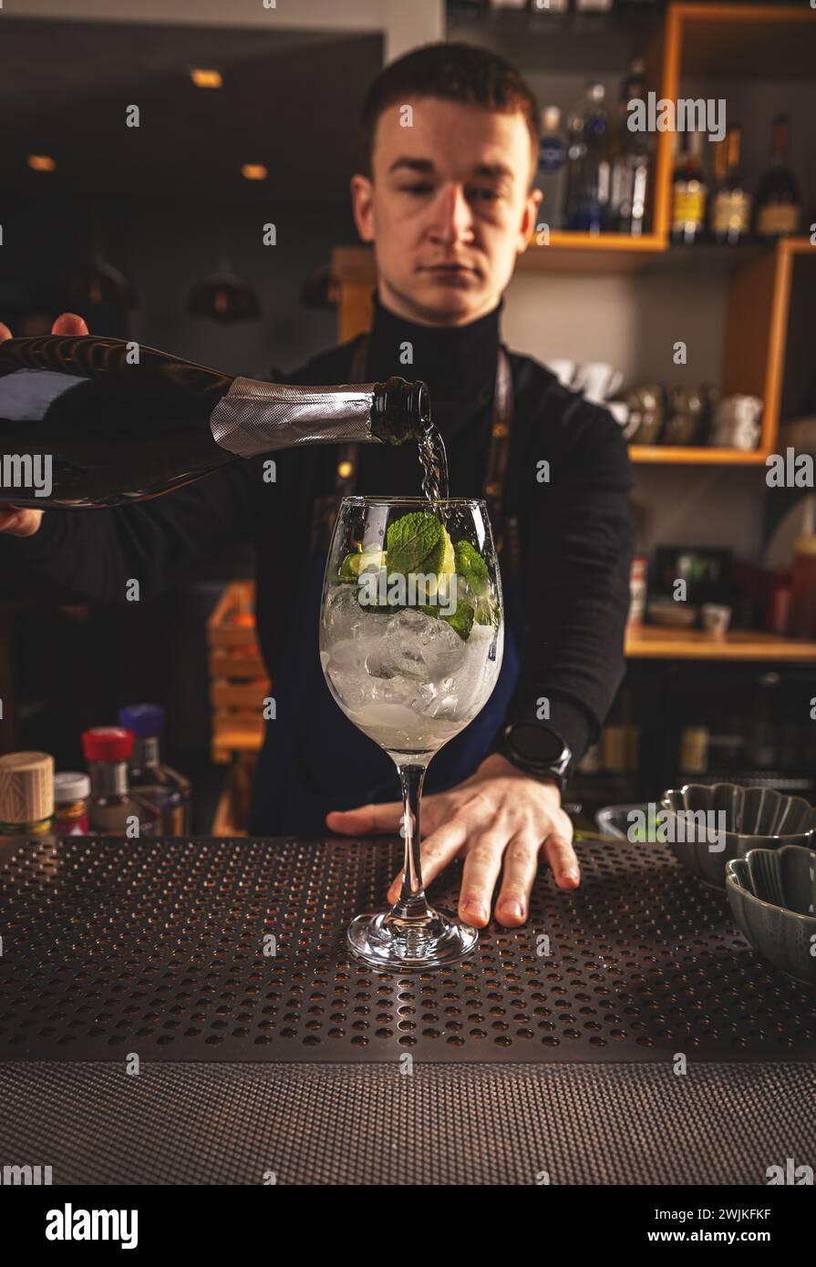 Bartender pouring champagne into glass full of ice cube decorated with mint, preparing aperol ...
