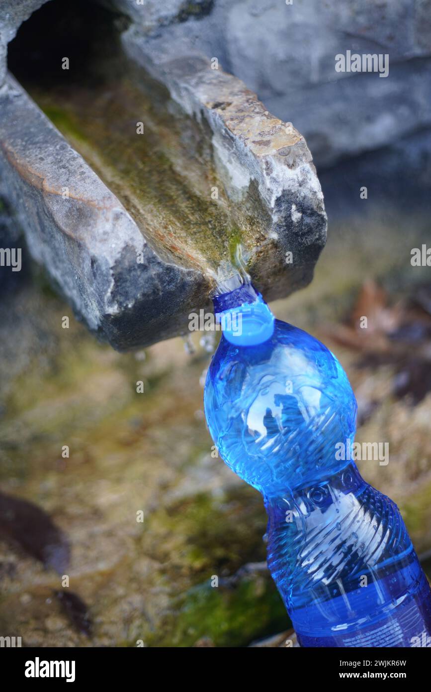 A person in a green sweater is collecting clean water into a plastic ...