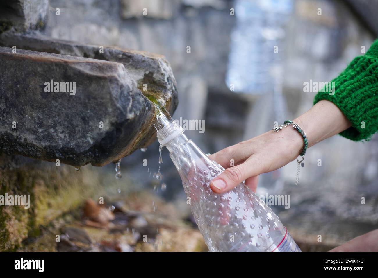 A person in a green sweater is collecting clean water into a plastic ...
