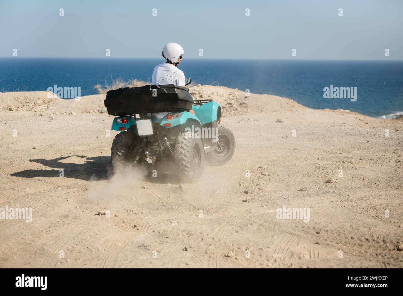 Young man riding four wheeler ATV on rocky path overlooking seashore ...