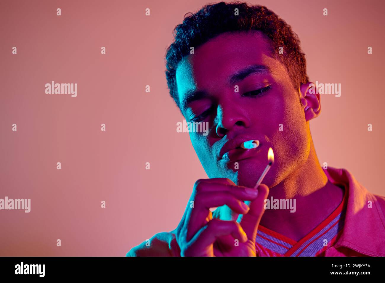 african american guy lighting a cigarette with match under blue neon ...