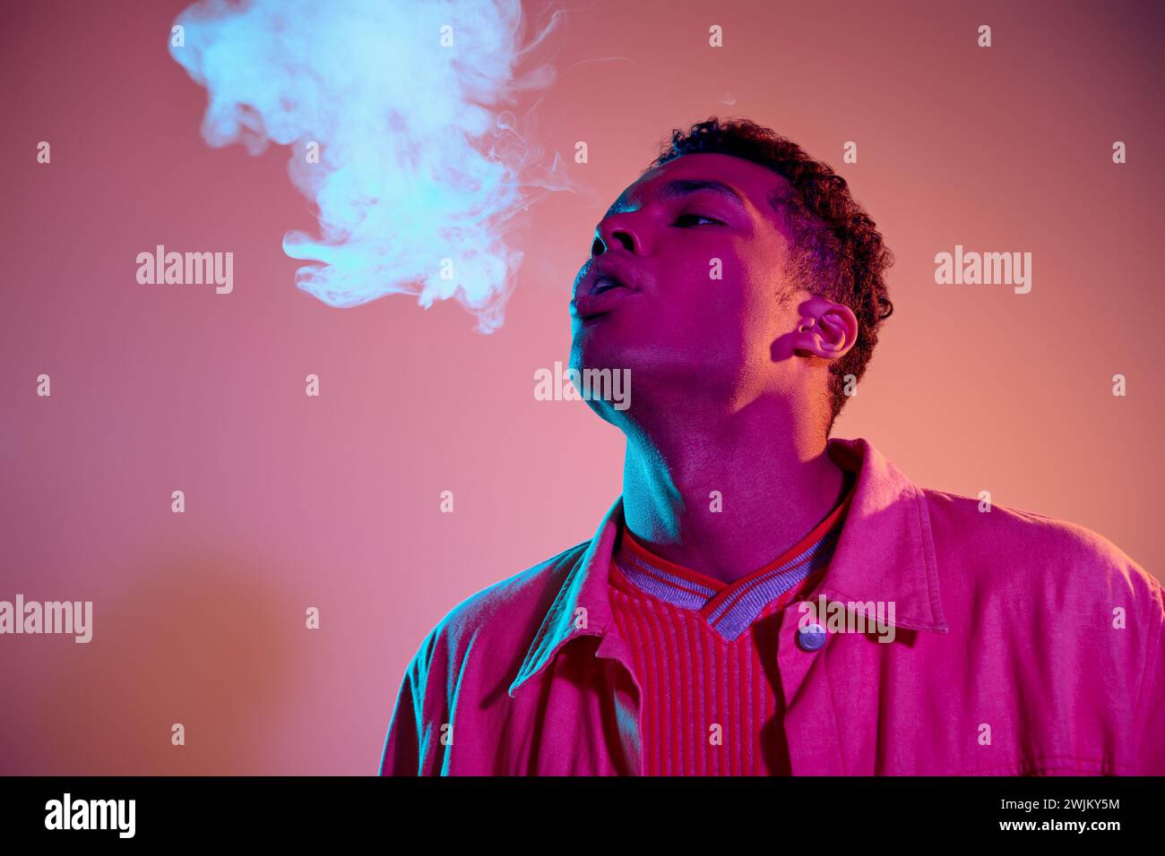 portrait of african american man exhaling smoke against vibrant ...