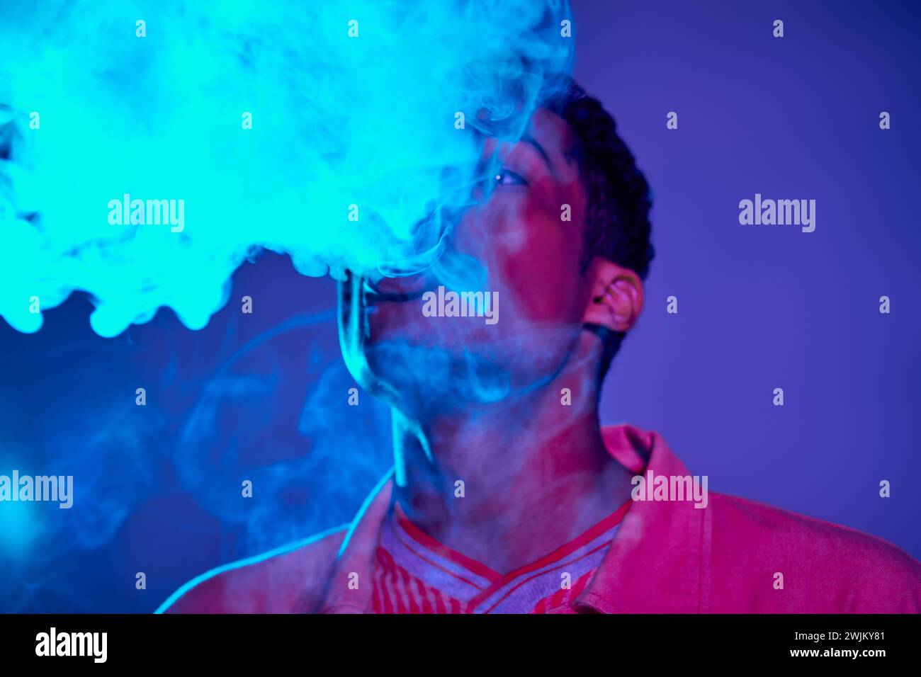 portrait of african american guy exhaling smoke against blue background ...
