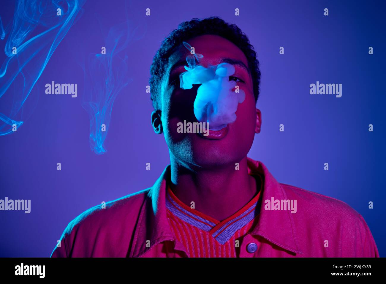 stylish african american guy exhaling smoke against blue background ...
