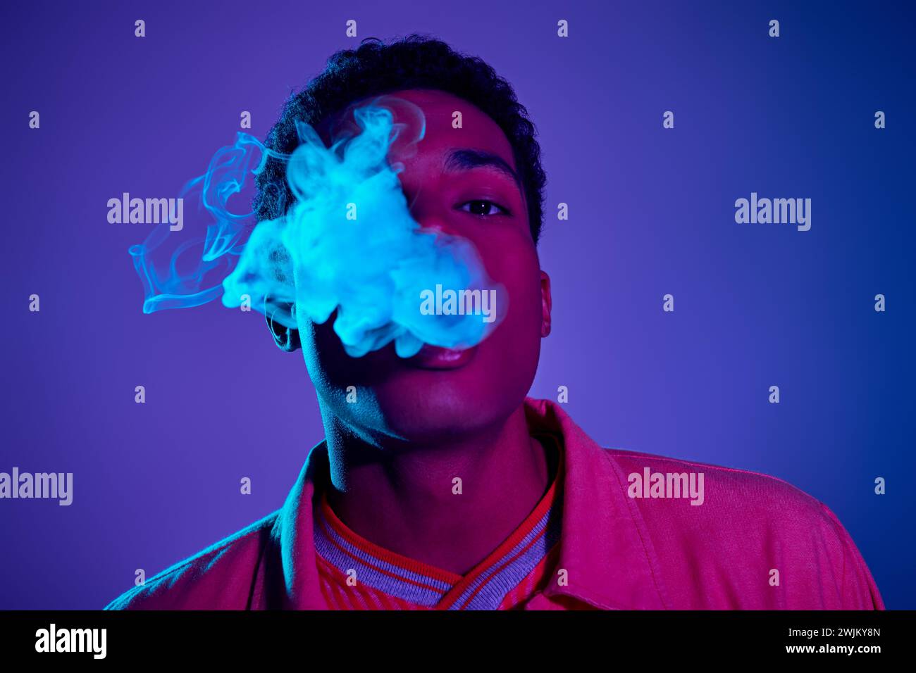 young african american man exhaling smoke against blue background with ...