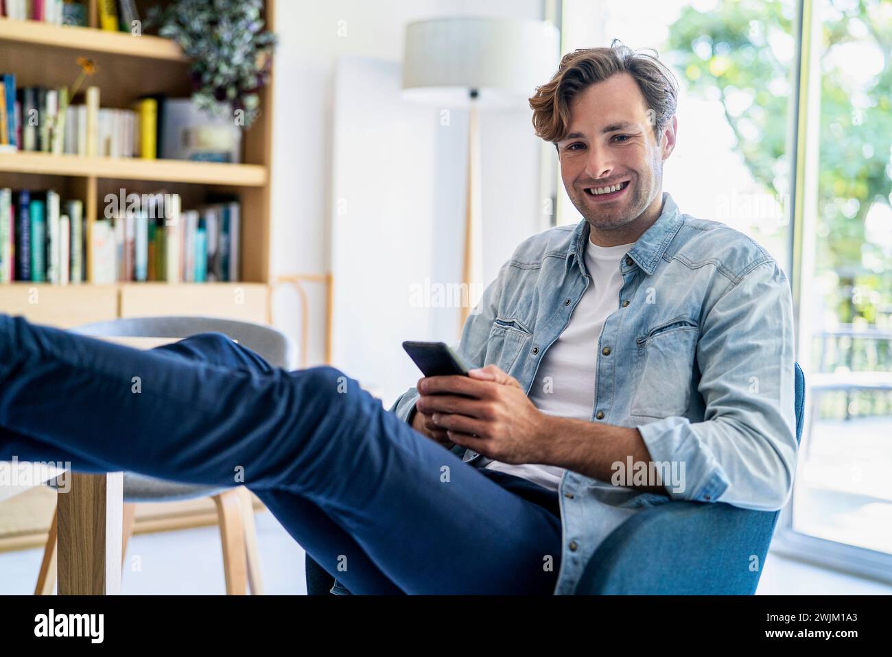 Businessman using smart phone while sitting on chair with feet on table ...
