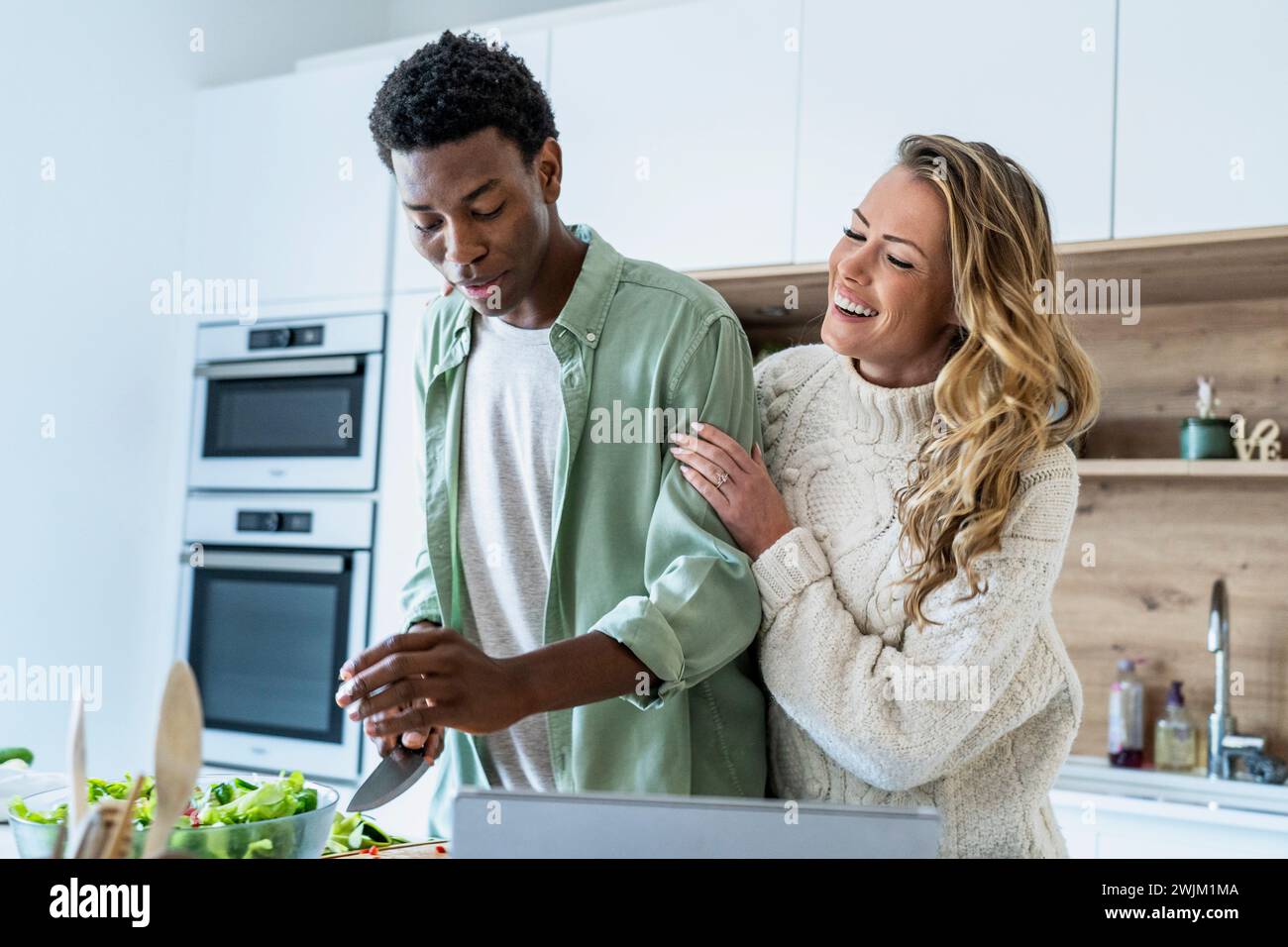 Adult woman embracing boyfriend while cutting vegetables at kitchen ...