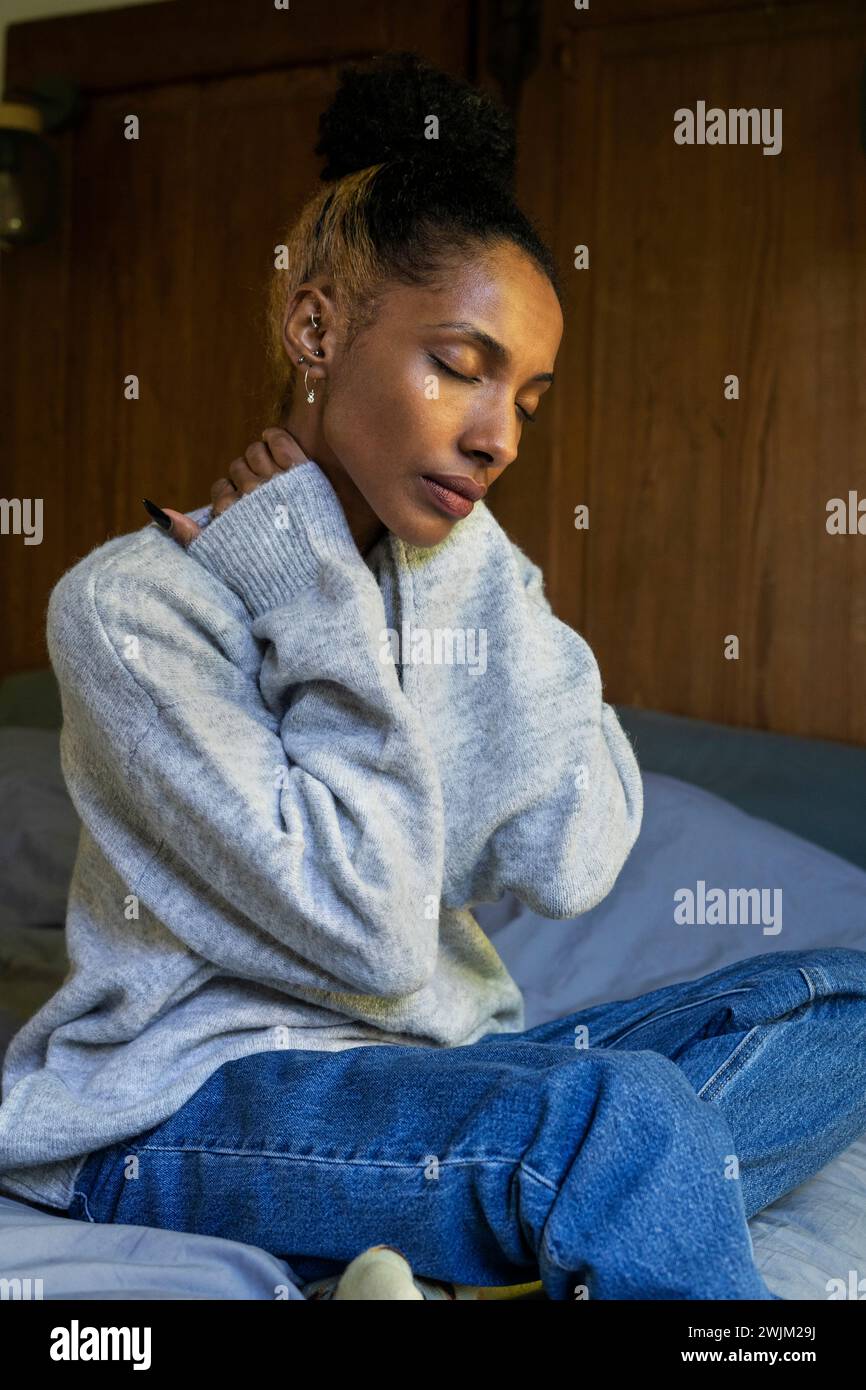 Stressed young adult woman touching her neck while sitting on bed Stock ...