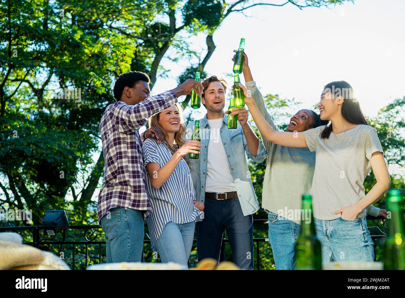 Five friends raising beer bottles while toasting during rooftop party ...