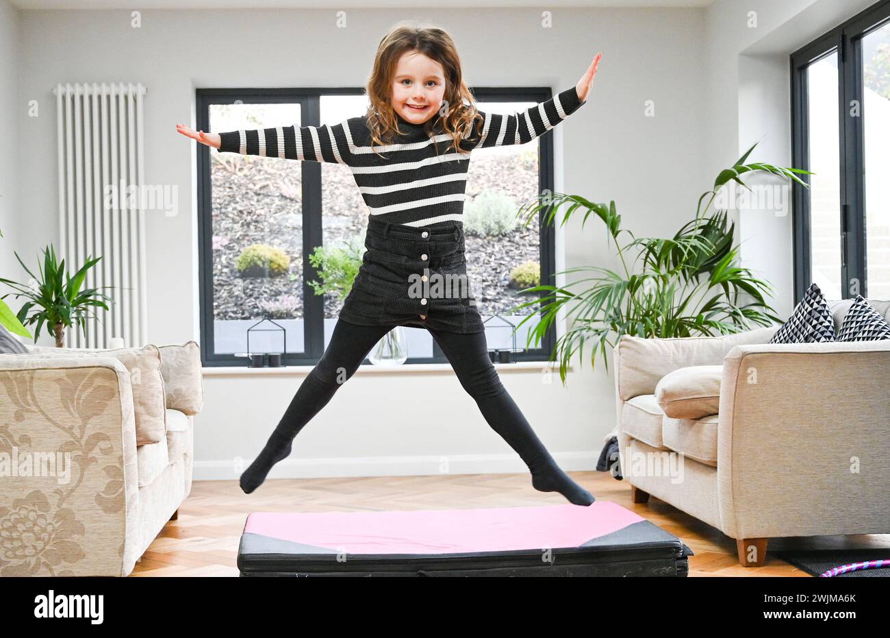 Young 7 year old girl doing a star jump in her home to keep fit and ...
