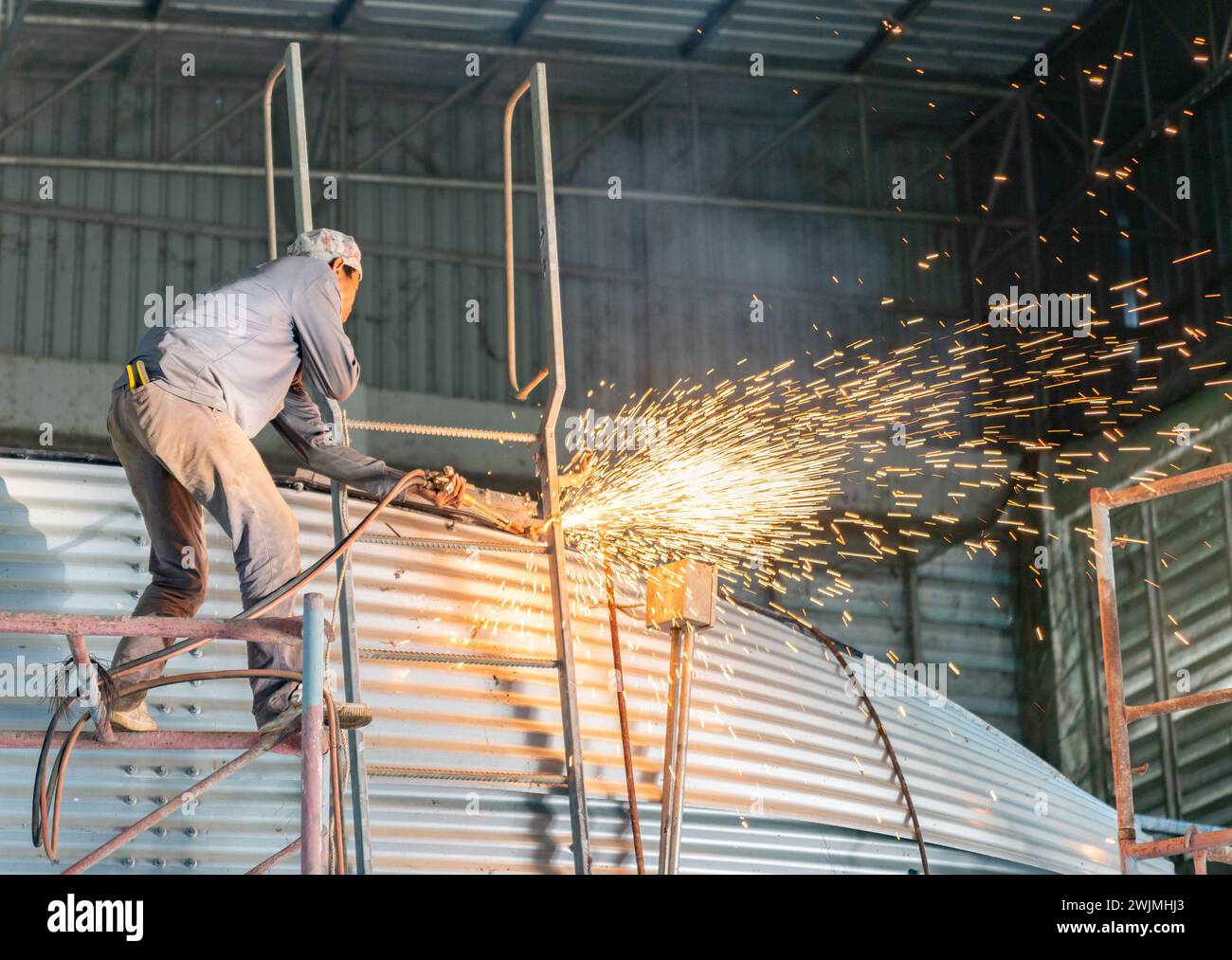 Worker use gas torch cutting metal sheet wall of water tank in factory ...