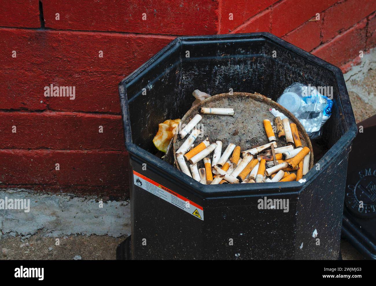 Cigarette ends in a container outside a bar Stock Photo - Alamy