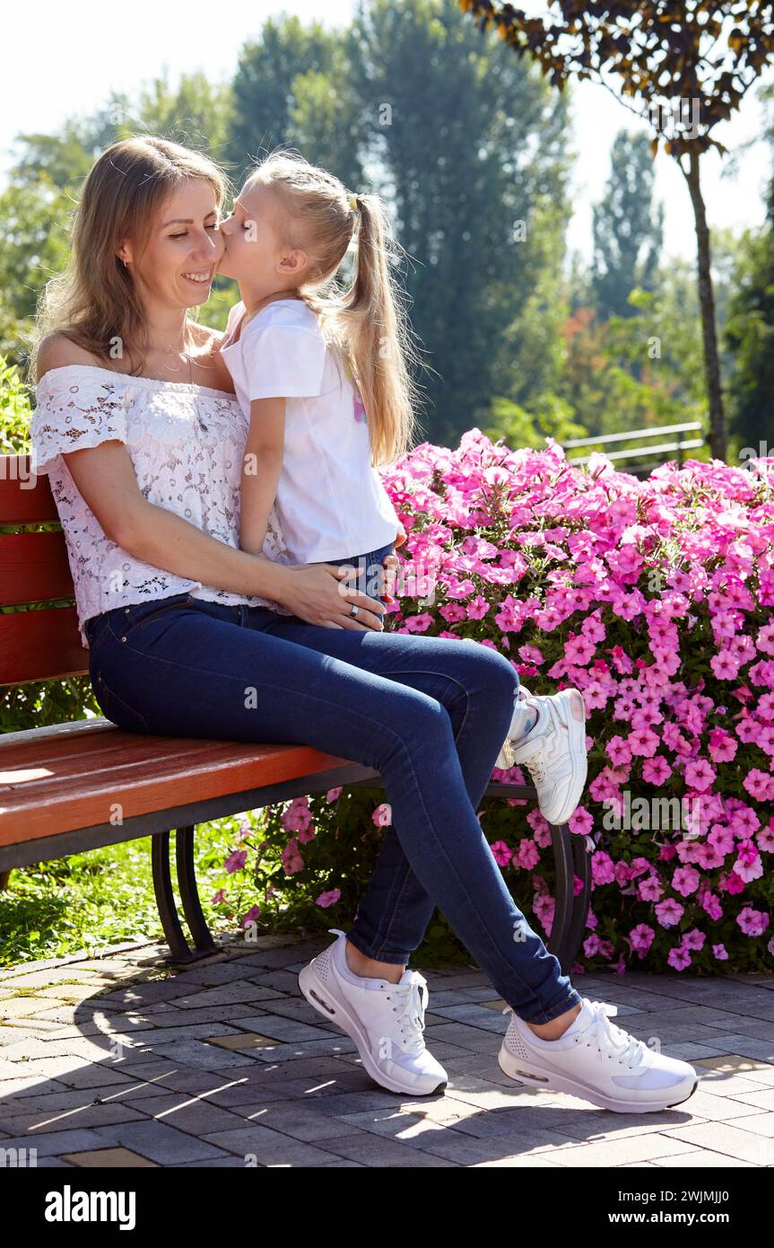 Mother and daughter sitting on a bench in the summer city park. Childhood, leisure and people ...
