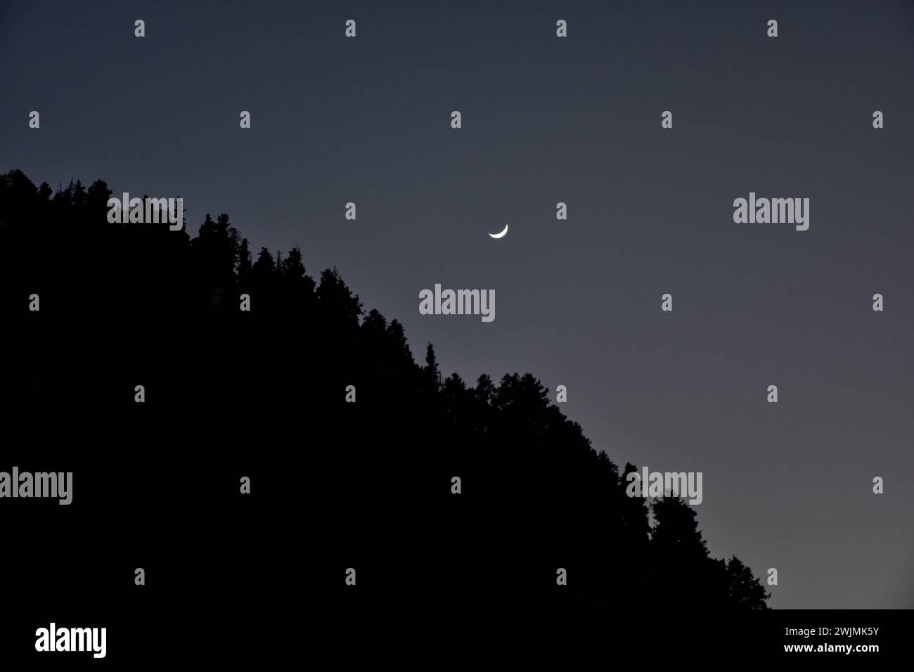 The waxing crescent moon rises over the mountain on the outskirts of ...