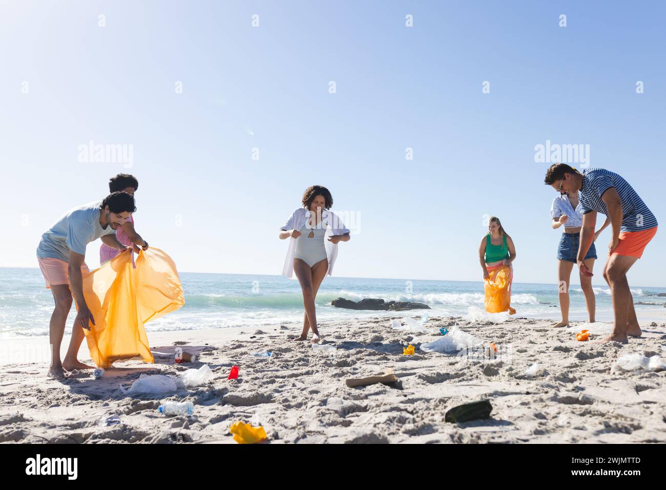 Diverse friends, part of a group, clean up a littered beach, collecting ...