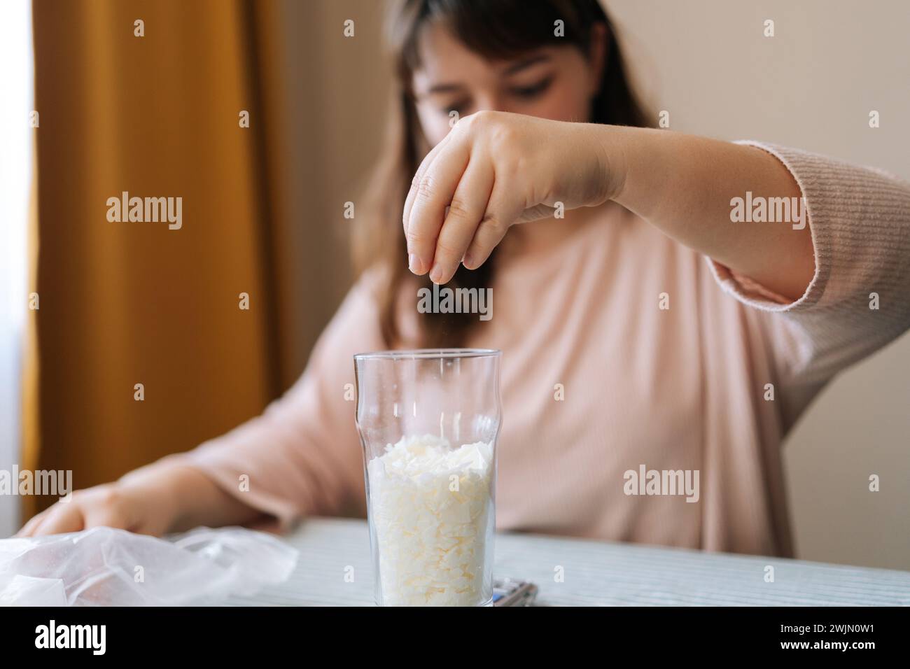 Close-up hands of focused female artisan pouring dry mixture or soy wax ...
