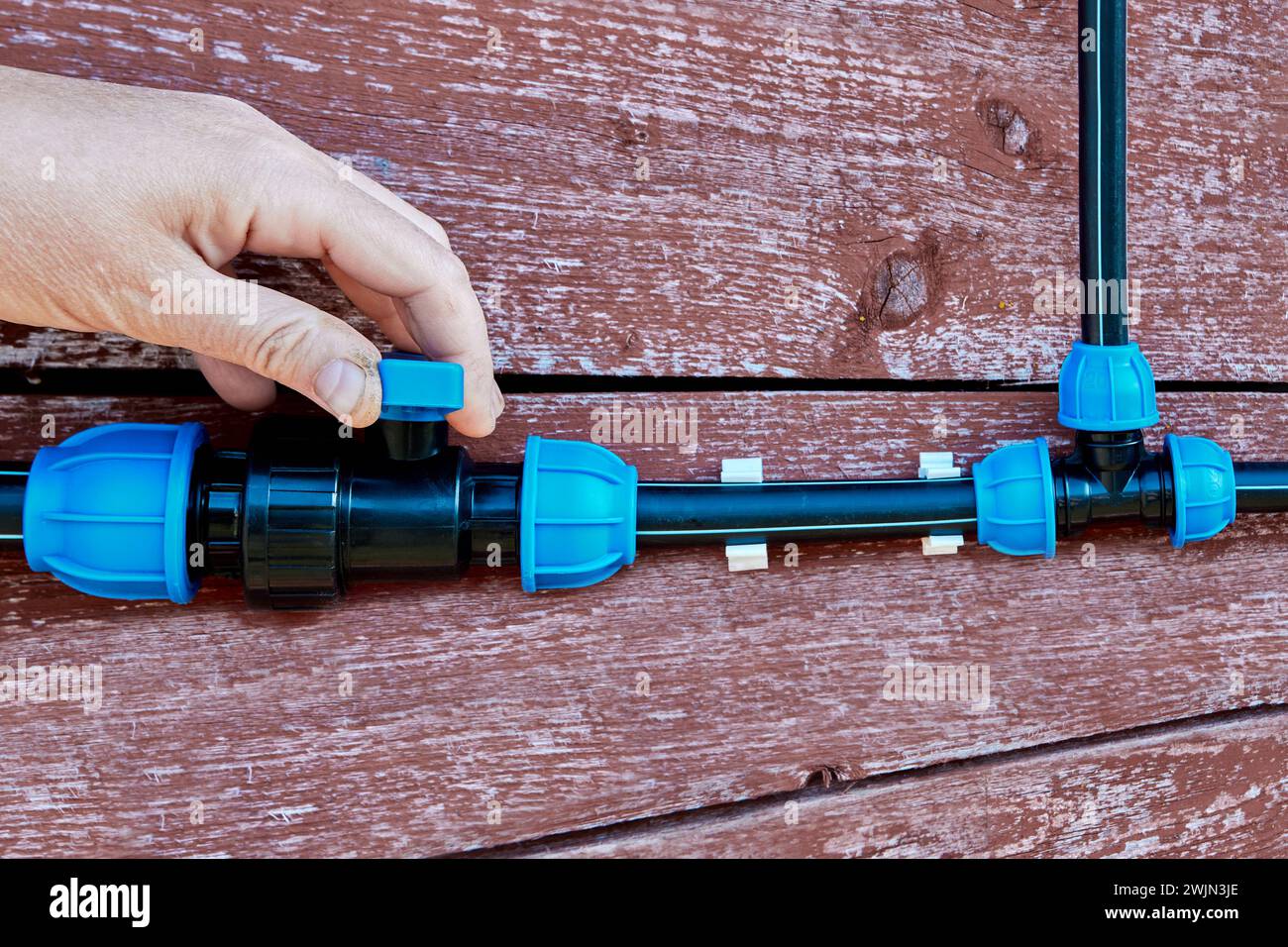 Closeup of hand shutting off water supply to an outdoor plastic water ...