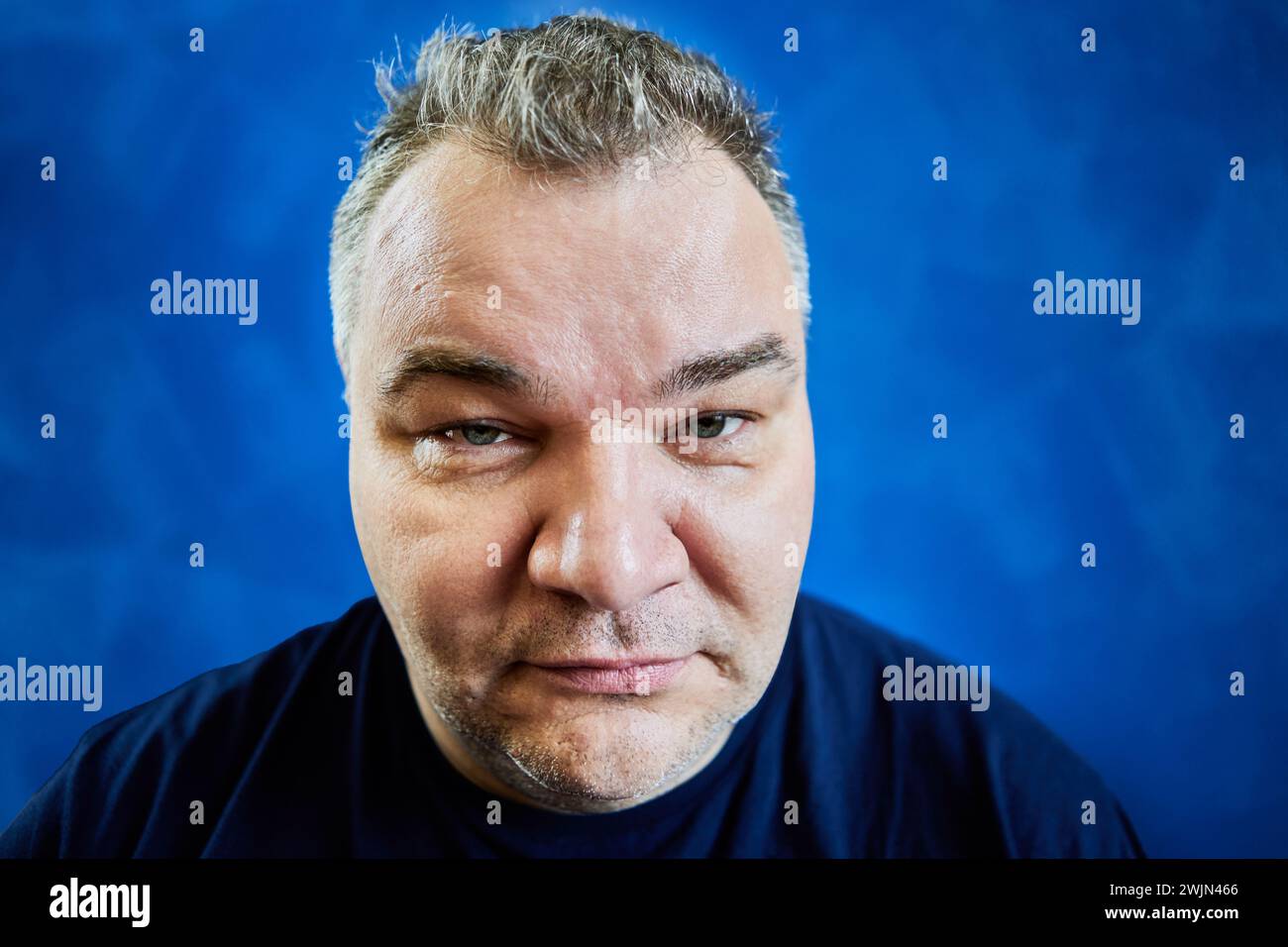 An appraising look of fat Caucasian man over 40, face close-up on blue ...