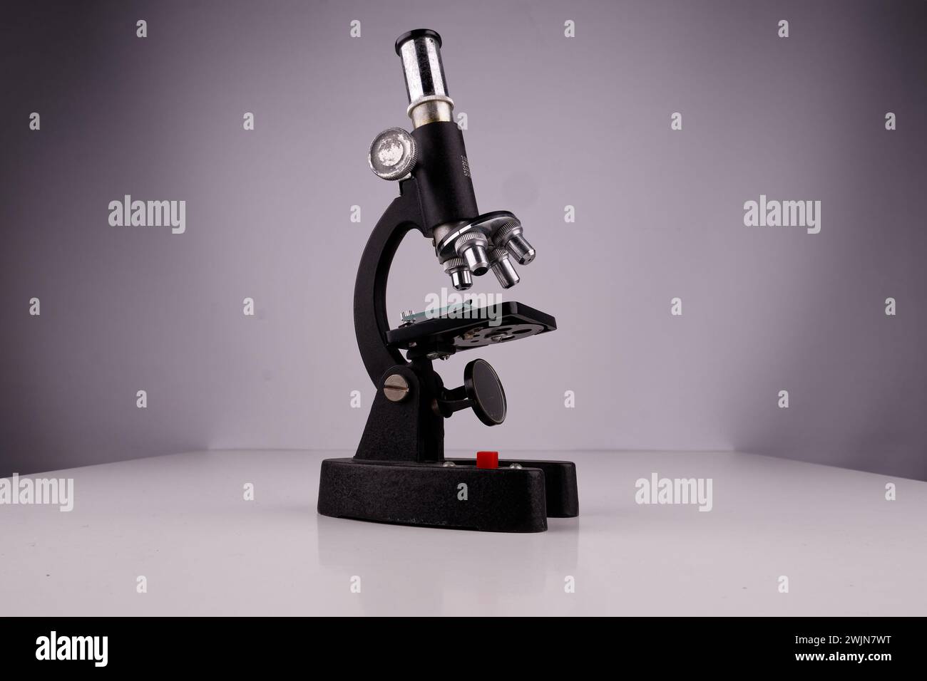 an old microscope stands on a white surface with real shadows, close up ...