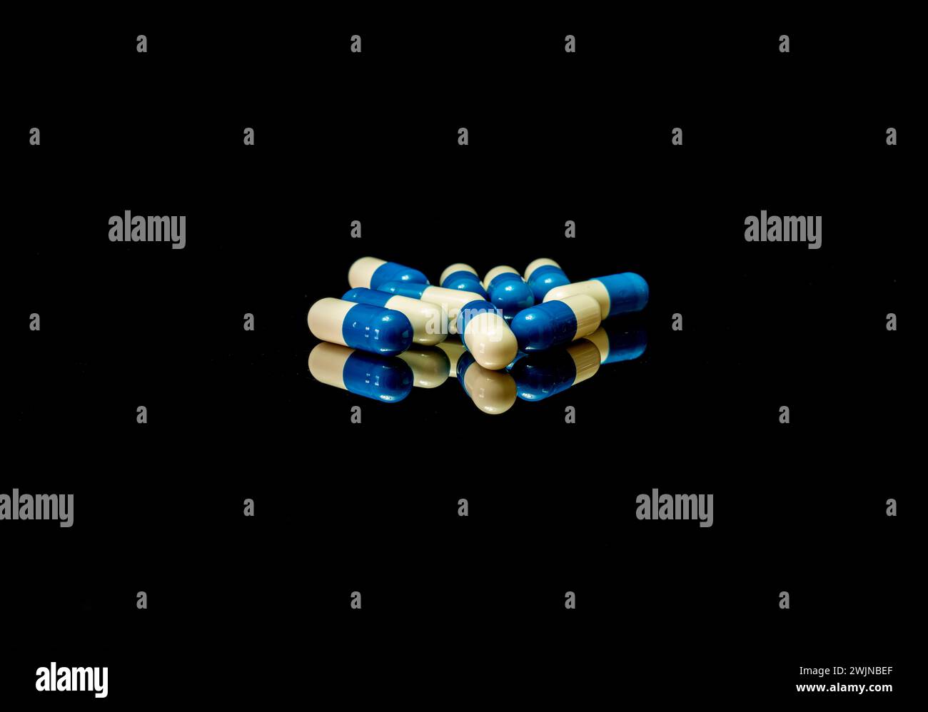 white and blue vitamin pills on a black background with reflection ...