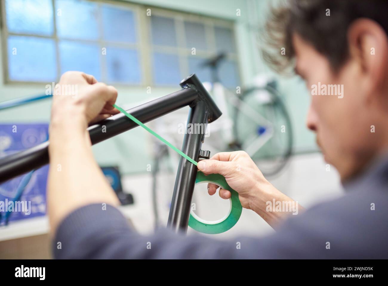 Hispanic man preparing a bicycle frame with masking tape for a custom ...