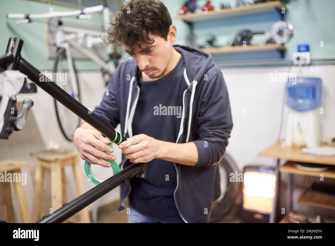 Hispanic young man preparing a bicycle frame with masking tape for a ...