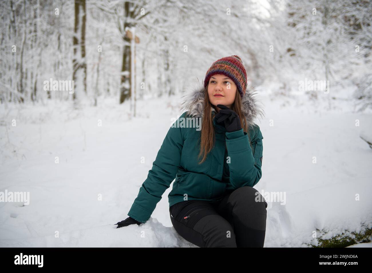 An image featuring a woman seated on a snow-covered ground in a forest ...
