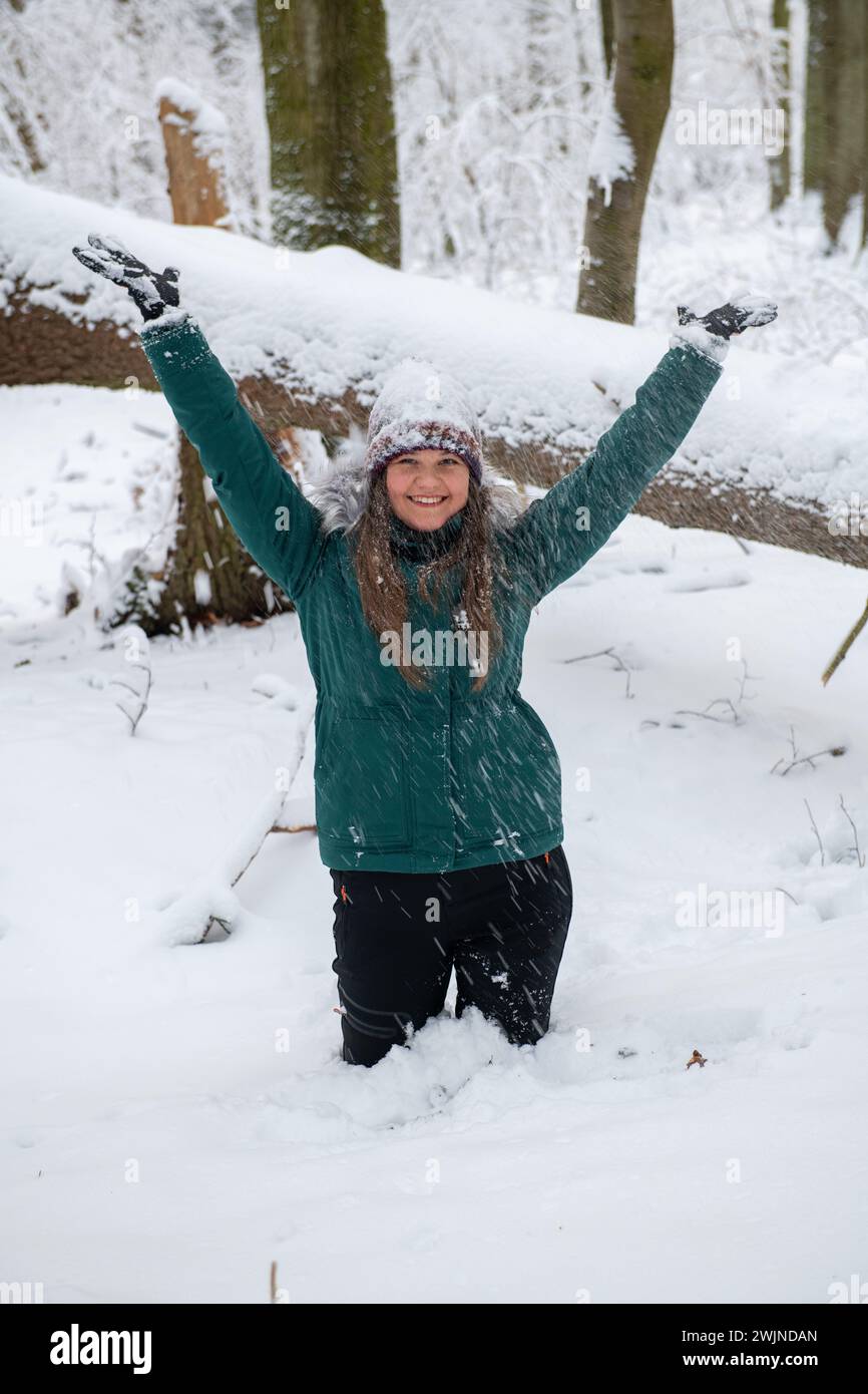 A woman in a teal winter coat with her arms joyfully raised amidst a ...