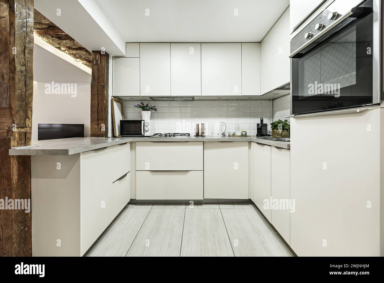 An open kitchen with white wooden furniture, appliances built into a ...